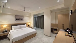 Quarto de hotel com uma cama grande, luminárias laterais, uma escrivaninha com cadeira e um guarda-roupa.