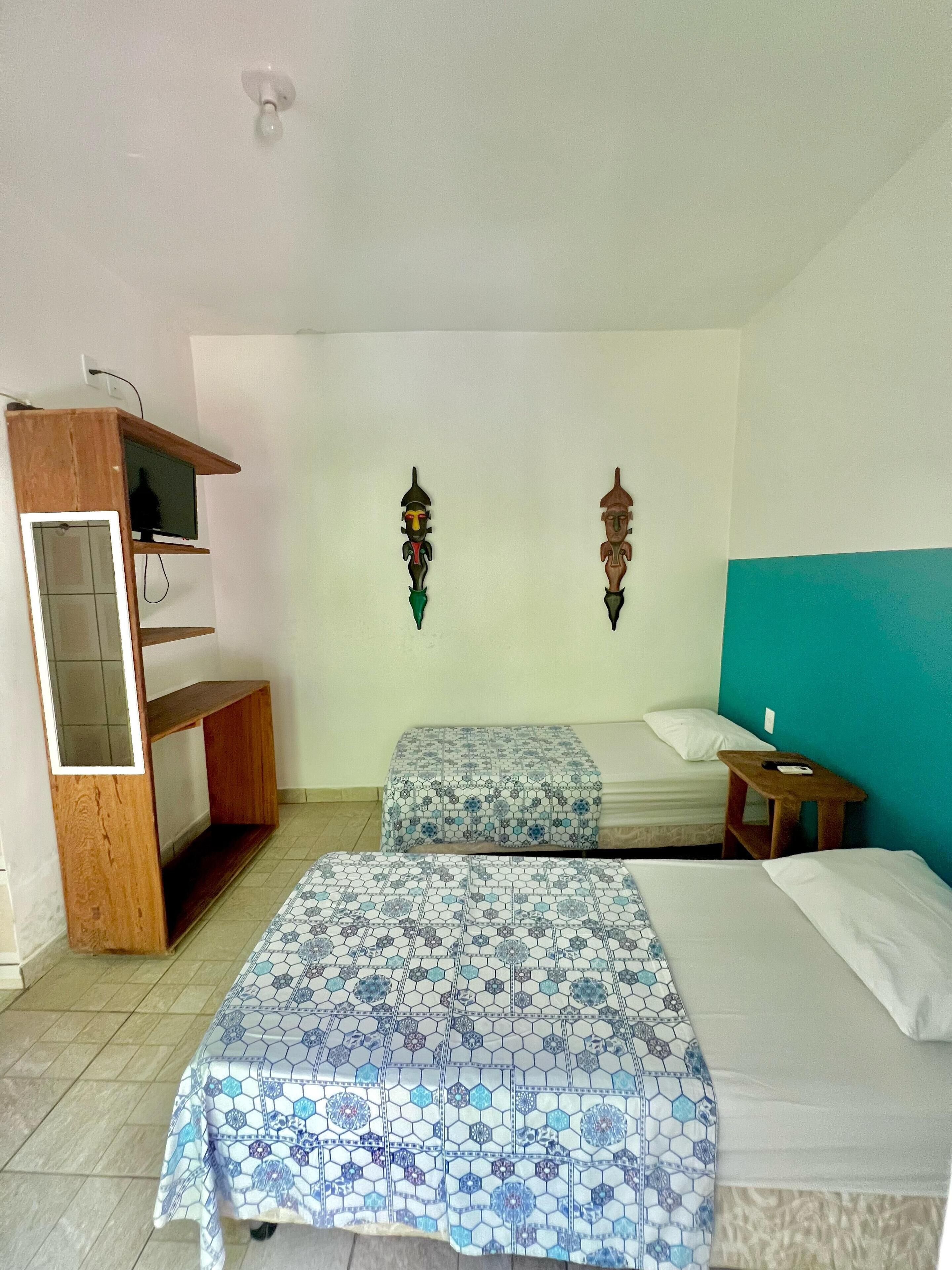 Quarto com duas camas, uma estante de madeira com uma televisão e detalhes decorativos nas paredes.