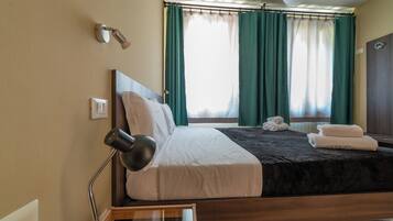 Uma cama bem arrumada com lençóis brancos, um abajur e um cobertor escuro.