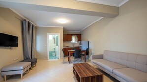 Sala de estar com sofá, mesa de centro e televisão. Cozinha integrada com armários e geladeira.