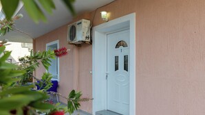 Um edifício com porta branca, ar condicionado na parede e um pequeno alpendre com uma cadeira.