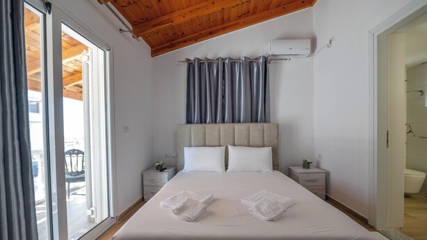 Quarto com uma cama grande, duas mesas de cabeceira, uma cabeceira e uma porta de vidro deslizante para área externa.