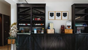 Uma área de recepção com um balcão de madeira escura, garrafas de vinho, certificados emoldurados e uma máquina de café.