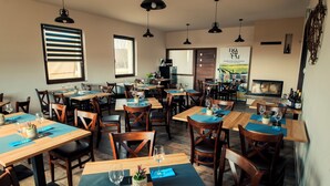 Restaurante com várias mesas e cadeiras, cada conjunto com um apoio para prato, taça de vinho e uma pequena planta.