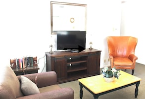 Uma sala de estar com televisão, sofá, poltrona, mesa de centro e estante de livros.