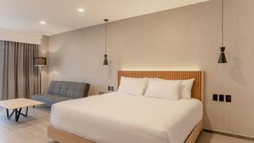 Quarto de hotel moderno com uma cama grande, um sofá, uma pequena mesa e luminárias pendentes.