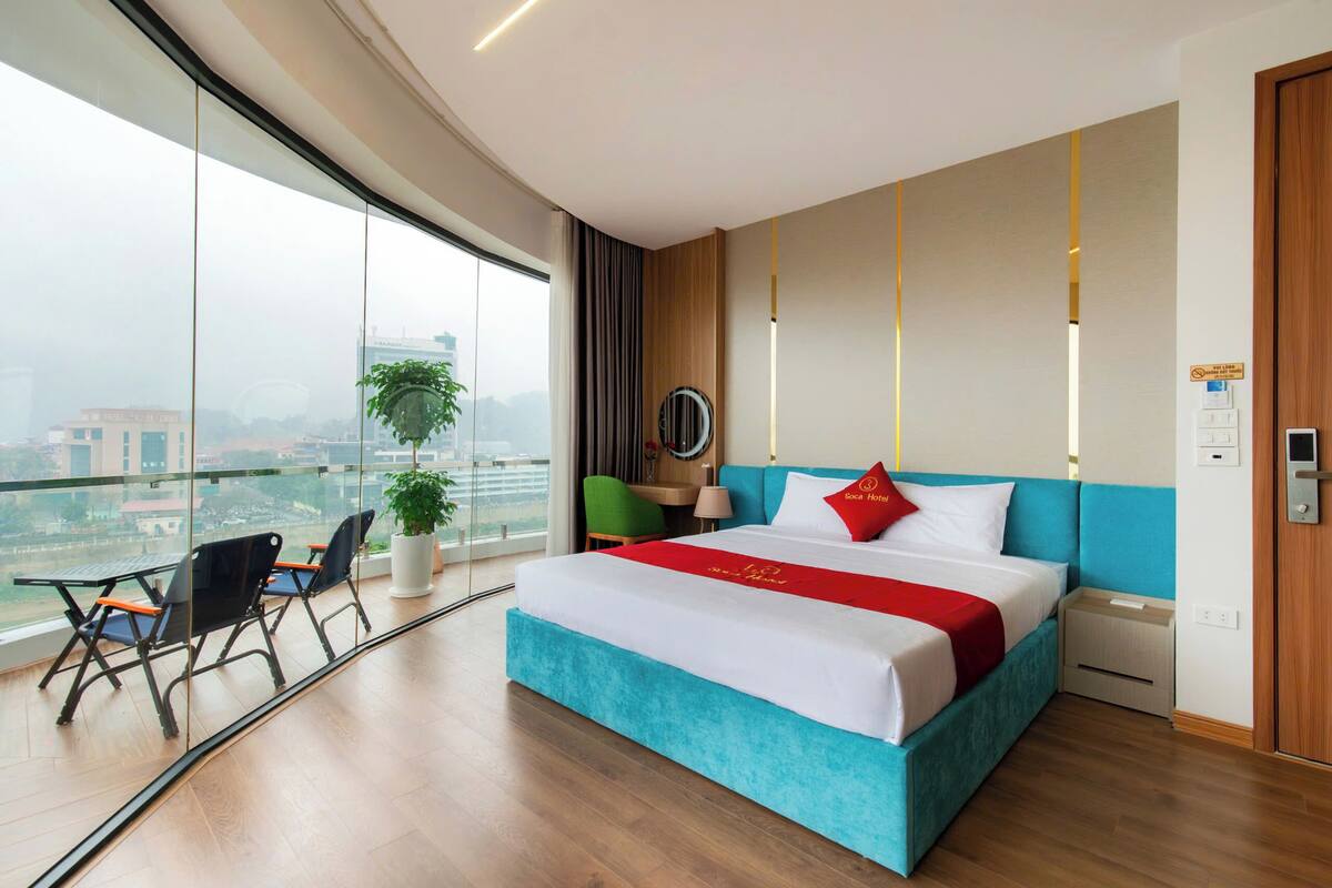 Quarto de hotel moderno com uma cama grande, uma escrivaninha, uma cadeira e vista para a cidade.