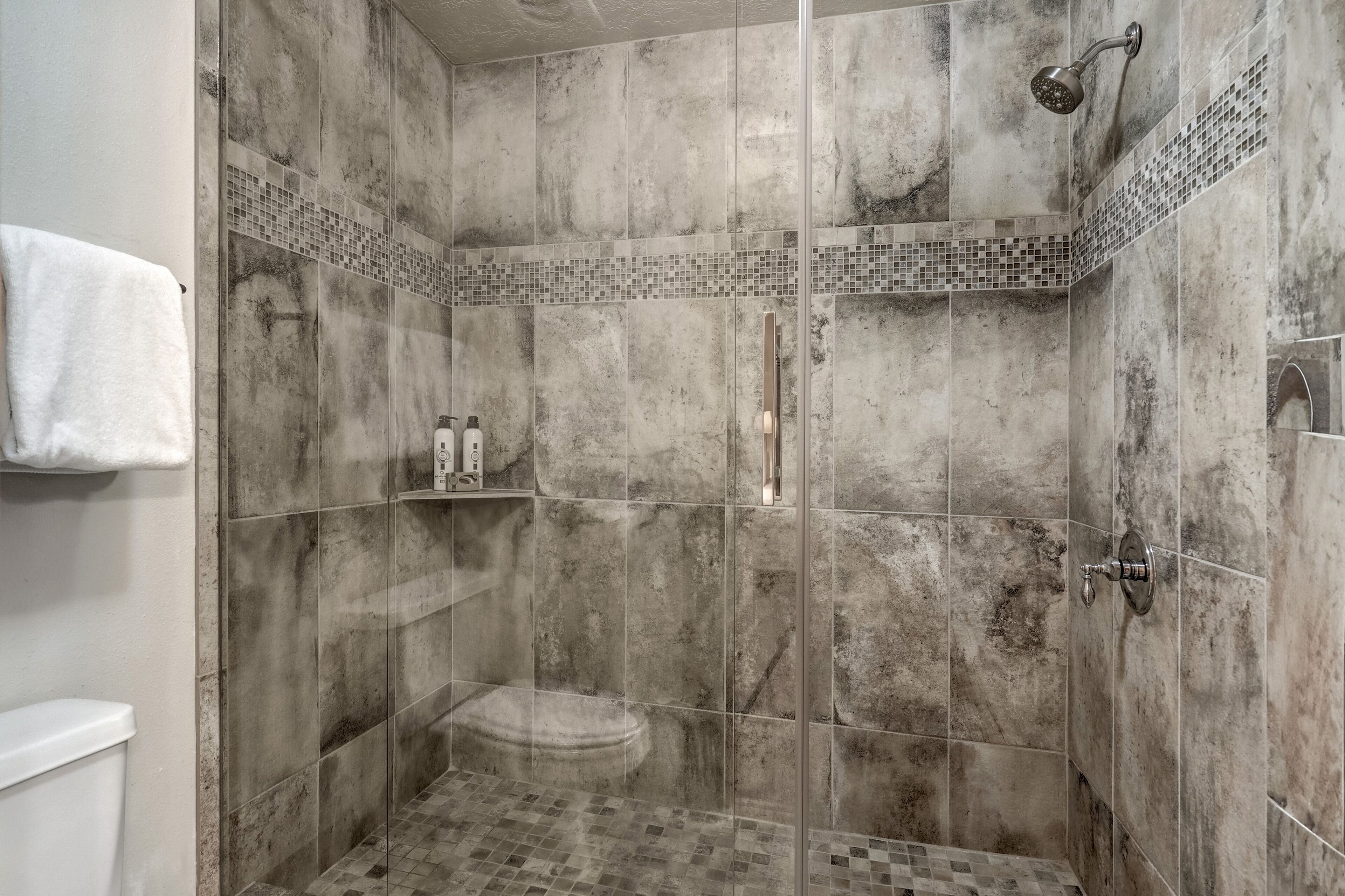 Um chuveiro com porta de vidro, paredes revestidas de azulejos e um pequeno nicho para produtos de higiene pessoal.