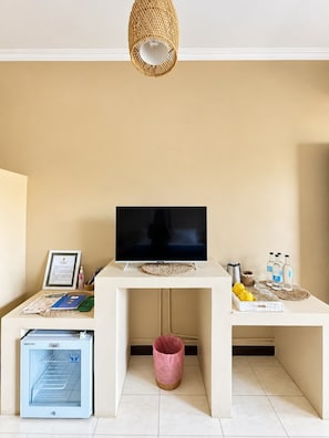 Uma sala de estar moderna com televisão de tela plana, um pequeno frigorífico, um cesto de lixo e uma máquina de café.