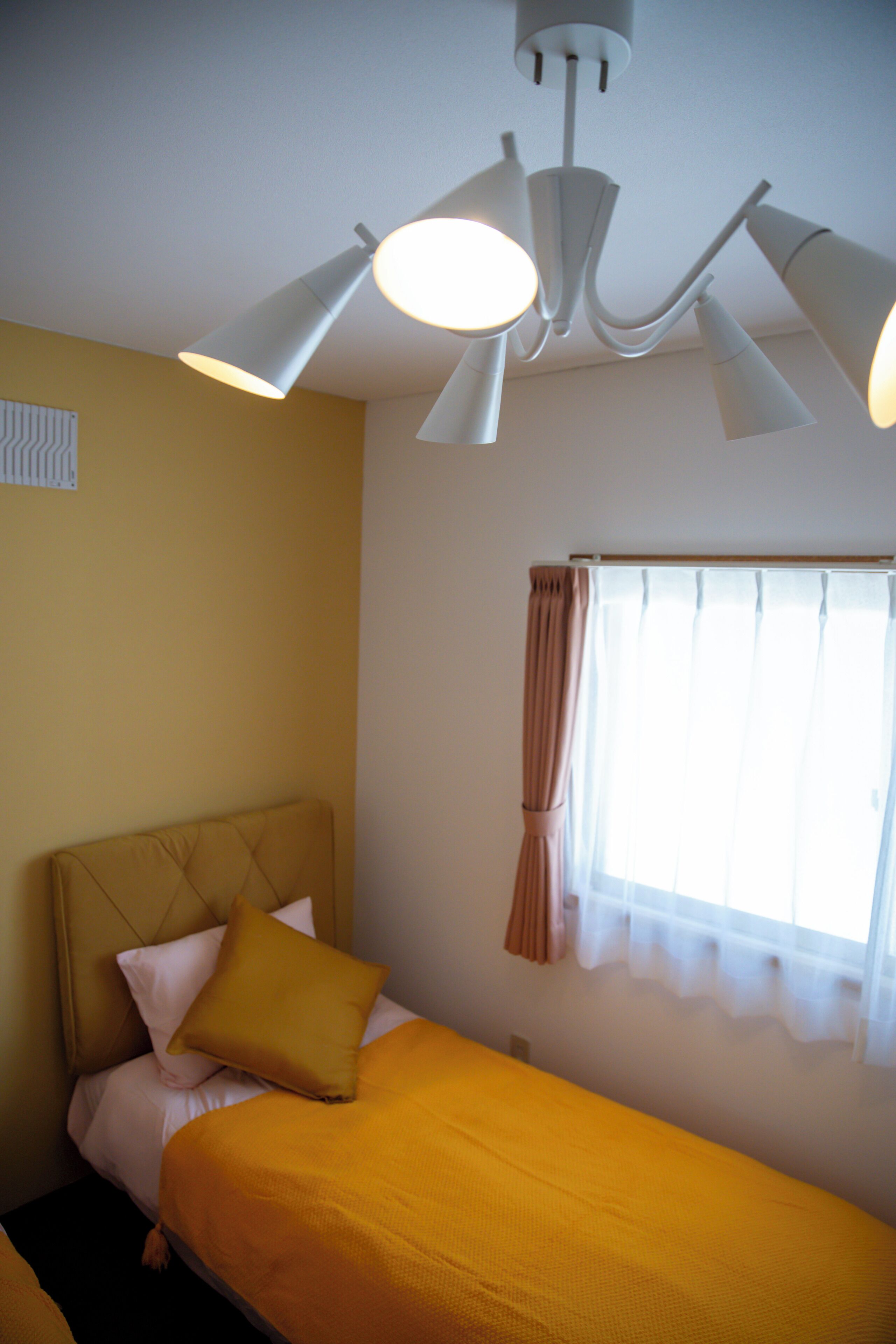 Uma cama de solteiro com cabeceira, mesa de cabeceira, janela com cortinas e luminária no teto.