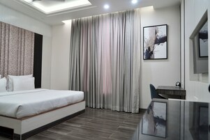 Quarto de hotel moderno com uma cama grande, uma escrivaninha e uma janela ampla com cortinas.