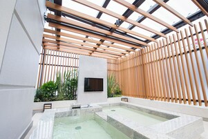 Uma área de spa com teto de ripas de madeira, televisão de tela plana e uma banheira de hidromassagem retangular.