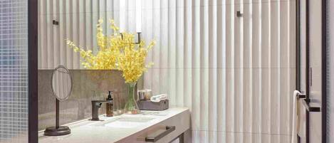 Um banheiro moderno com um espelho grande, um lavatório com pia, um vaso de flores amarelas e um porta-toalhas.