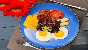 Prato com ovos, bacon, um tomate e vegetais sobre um prato azul.