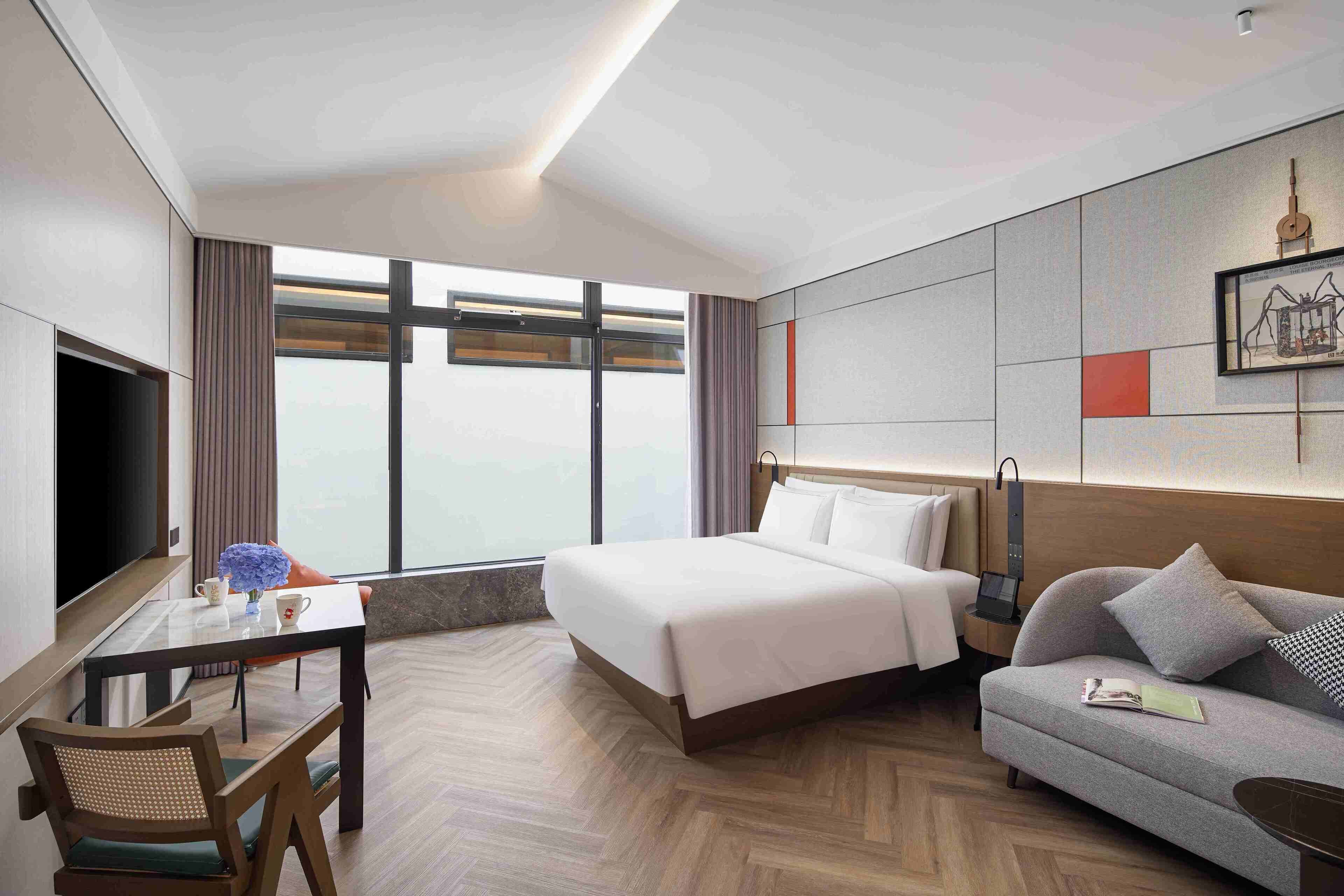 Quarto de hotel com uma cama, sofá, escrivaninha e televisão.