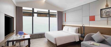 Quarto de hotel com uma cama, sofá, escrivaninha e televisão.