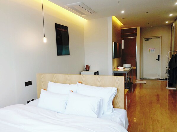 Quarto de hotel com cama, mesa de cabeceira, espelho, pia e porta que dá para um corredor.