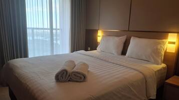 Quarto de hotel com cama bem arrumada, duas almofadas, cabeceira com iluminação integrada e janela com cortinas.