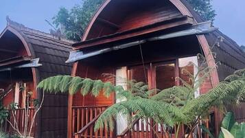 Uma fileira de cabanas de madeira com telhado de palha, cercada por vegetação exuberante e um caminho de pedra.