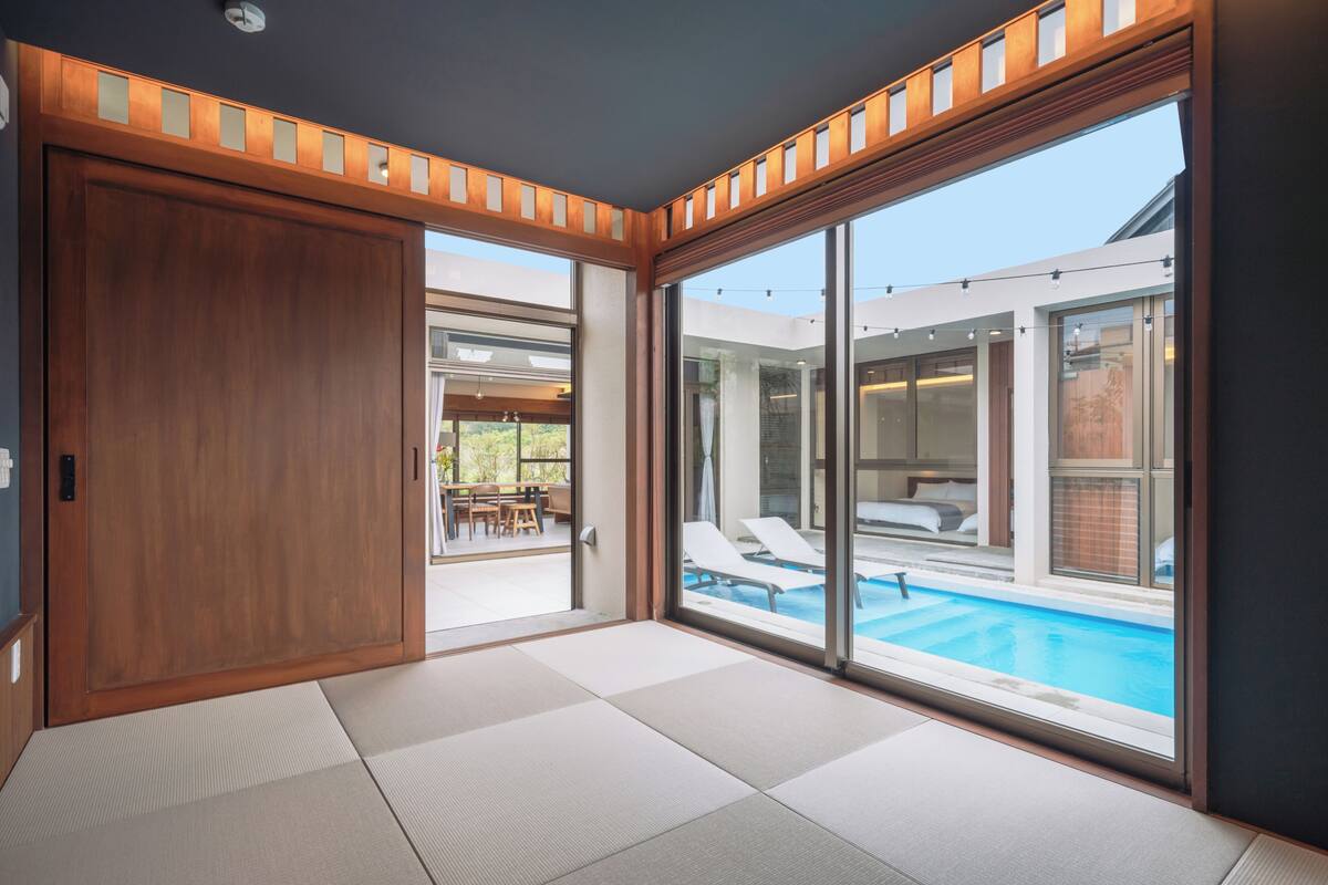 Quarto moderno com tatames e grandes portas de vidro deslizantes que dão para uma área de piscina.