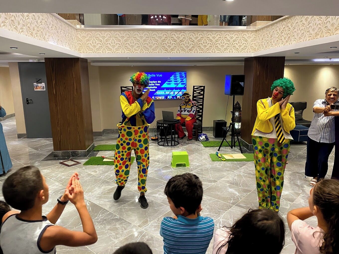 Um saguão de hotel com palco para apresentações, área de estar e balcão de recepção.