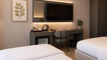 Quarto de hotel com cama, escrivaninha com cadeira, televisão e planta emoldurada na parede.