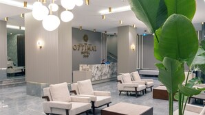 Um lobby de hotel moderno com balcão de recepção, área de estar e grandes plantas verdes.