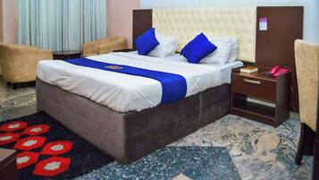 Quarto de hotel com uma cama grande, mesa de cabeceira, cadeira e tapete com padrão vermelho e azul.