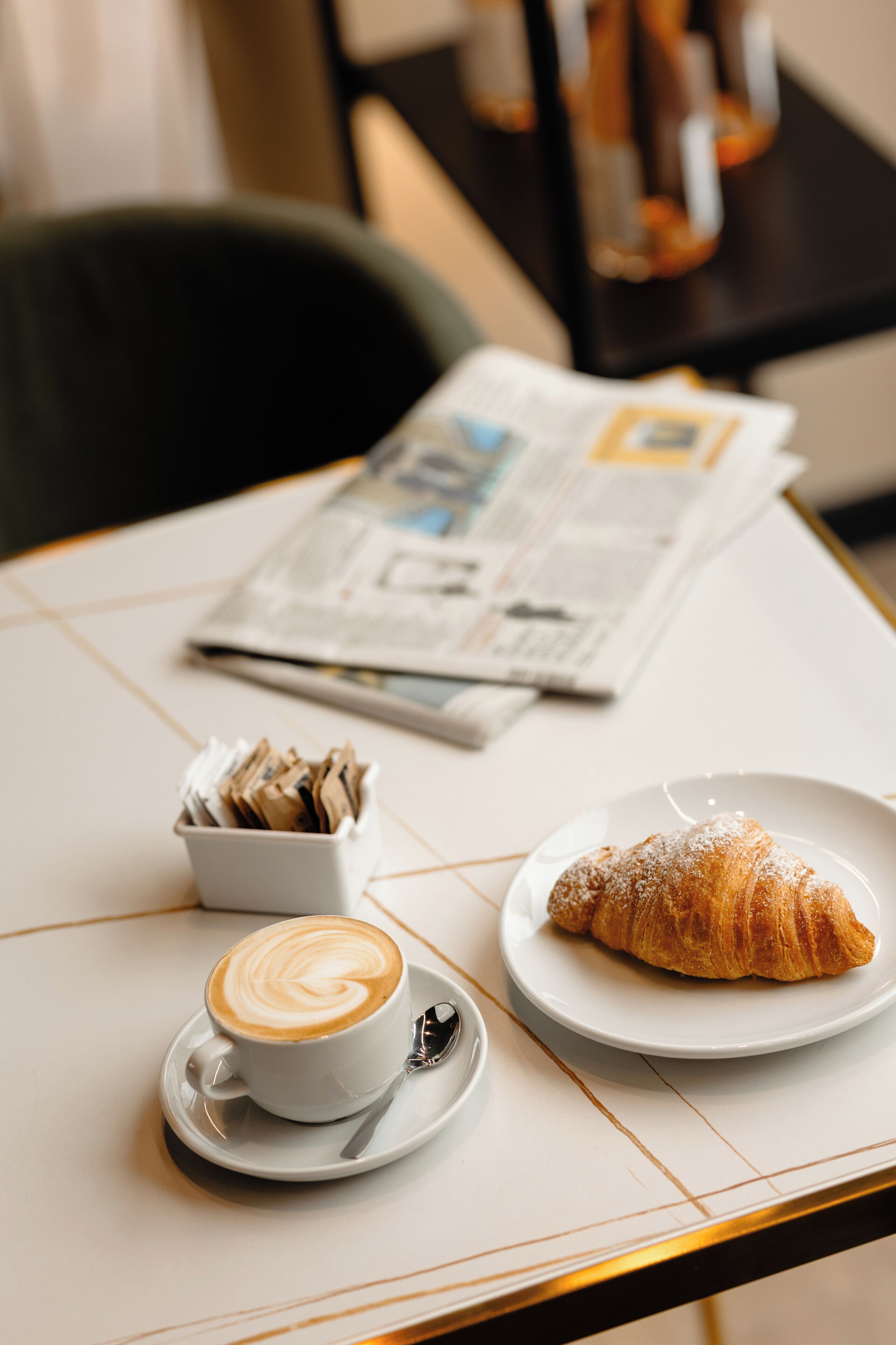 Uma mesa com um croissant, uma xícara de café e um recipiente com biscoitos.
