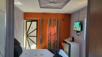 Quarto de hotel com cama, escrivaninha, televisão e janela com cortinas.