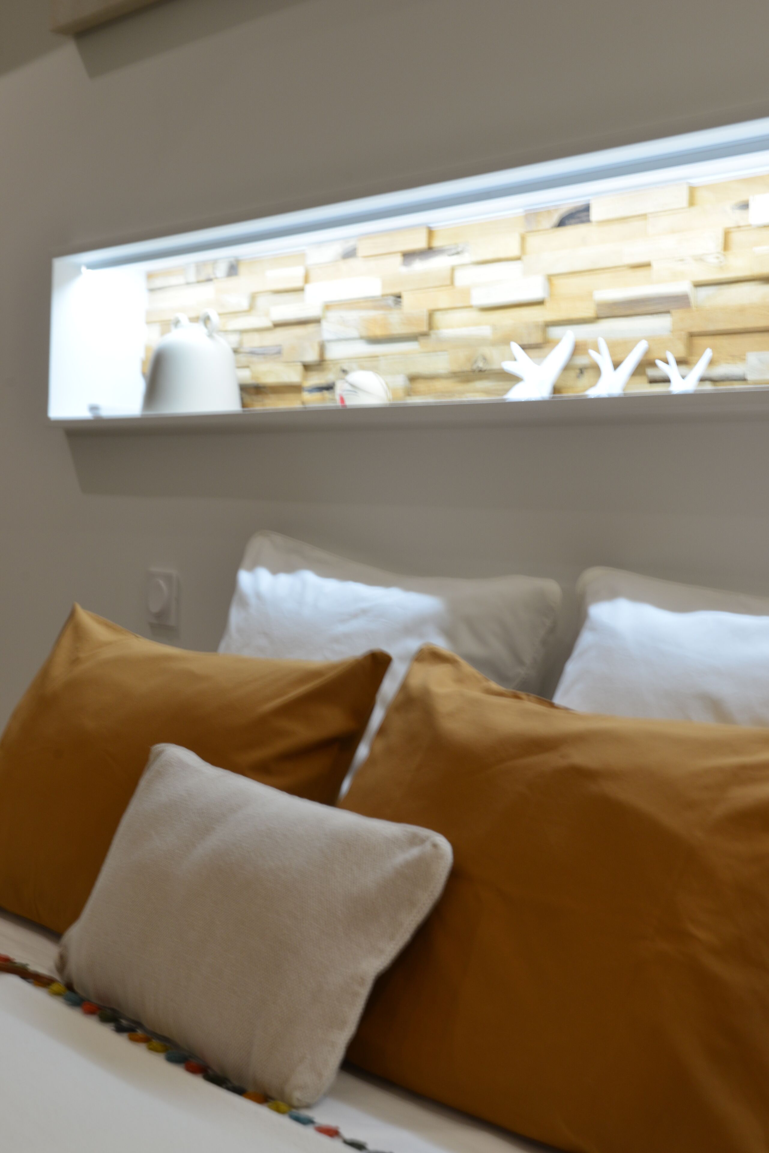 Quarto de hotel com cama, almofadas brancas e castanhas, e parede de madeira com espelho sobre a cama.
