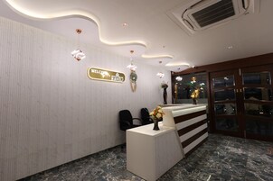 Uma área de recepção com design moderno, incluindo um balcão de atendimento, cadeiras, um letreiro de boas-vindas e iluminação decorativa.