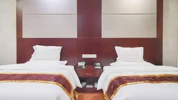 Quarto de hotel com duas camas, cabeceira de madeira, mesa de cabeceira e uma gaveta pequena.