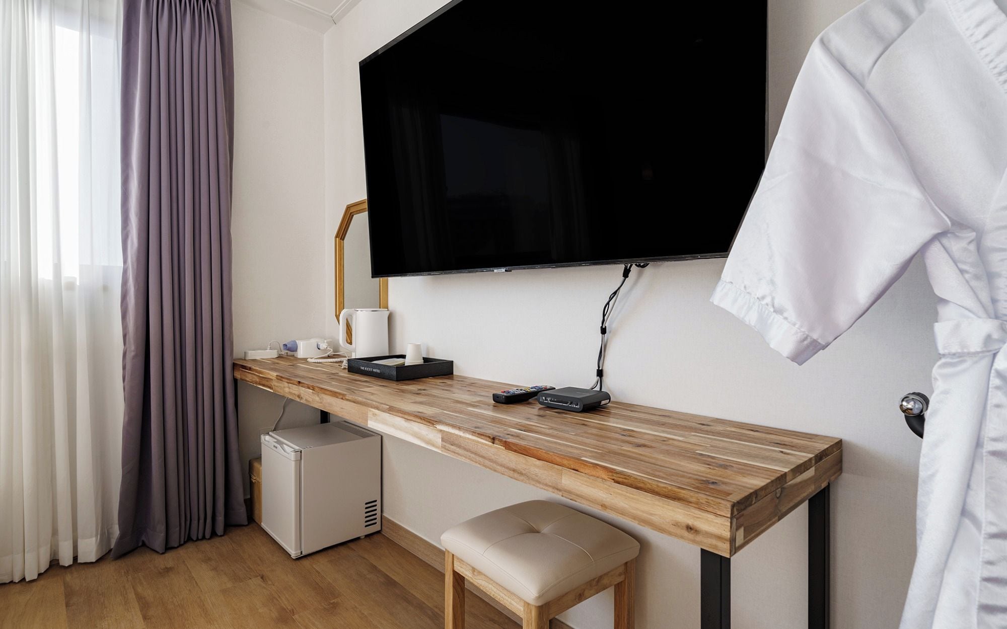 Quarto de hotel com escrivaninha de madeira, televisão de tela plana, mini-geladeira, cafeteira e controle remoto.