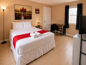 Quarto de hotel com cama, escrivaninha, cadeira, televisão, quadro e abajur.