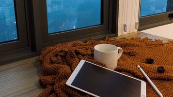 Ambiente acolhedor em interiores com um tablet, uma caneca e uma caneta sobre um cobertor de malha, com uma janela exibindo uma vista urbana.