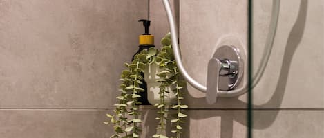 Casa de banho com chuveiro, dispensador de sabonete e planta em vaso.