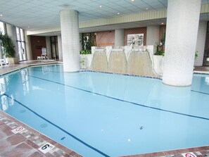 Uma piscina interior com água cristalina, rodeada por colunas e um chão em mosaico.
