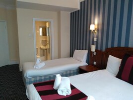 Quarto de hotel com duas camas de solteiro, uma cama de casal, banheiro com espelho e parede listrada.