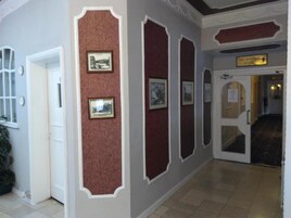 Um corredor com quadros nas paredes, uma porta à esquerda e uma placa acima de uma porta à direita.