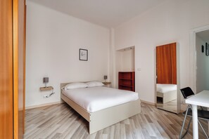Um quarto com cama, mesas de cabeceira, escrivaninha e guarda-roupa.