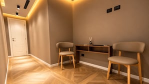 Um corredor com duas cadeiras, uma porta branca e um aparador de madeira.