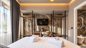 Quarto de hotel com uma cama grande, uma escrivaninha, uma cadeira, uma televisão e um banheiro.
