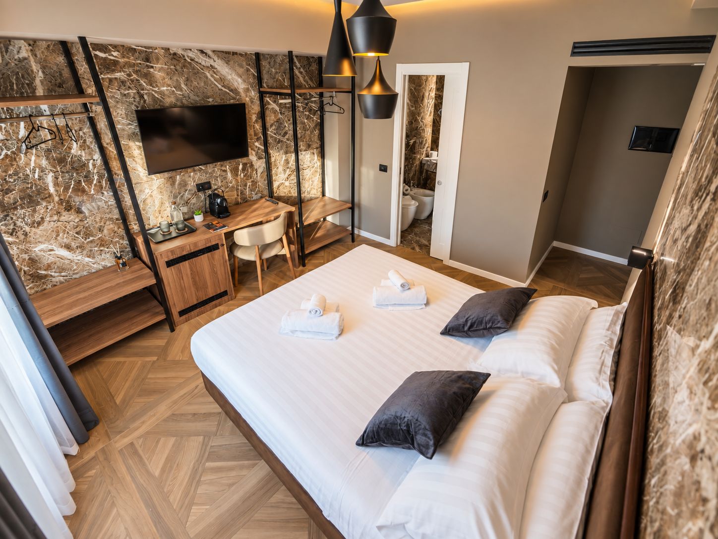 Quarto de hotel com cama, escrivaninha, televisão e banheiro visível por uma porta aberta.