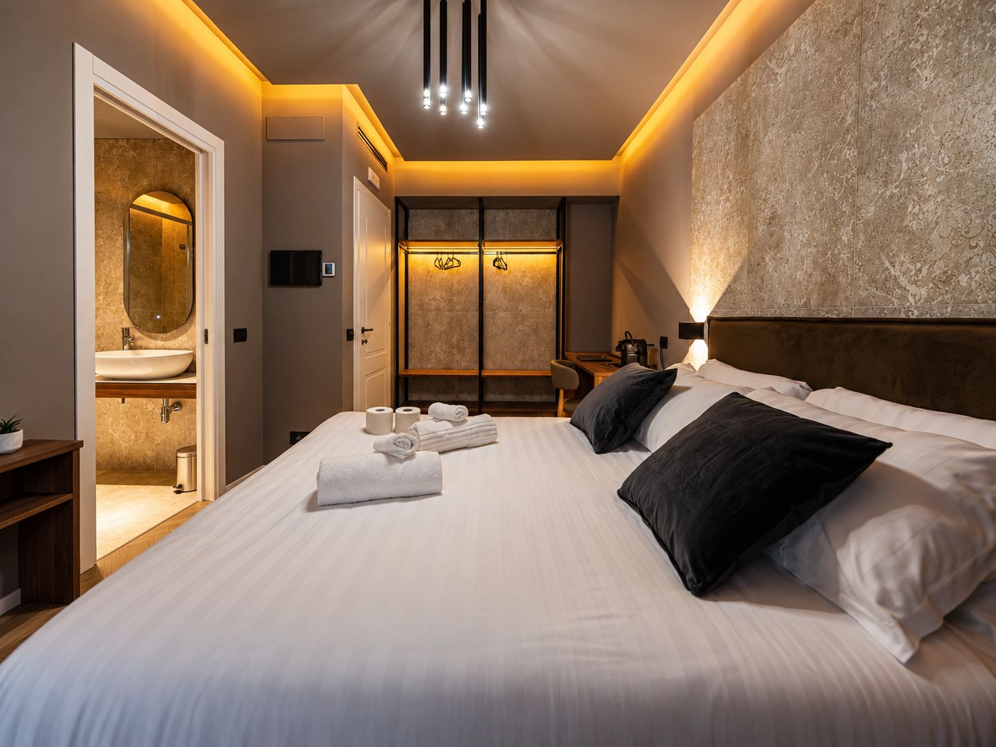 Quarto de hotel com cama grande, mesas de cabeceira, escrivaninha, cadeira, espelho e banheiro com pia e vaso sanitário.
