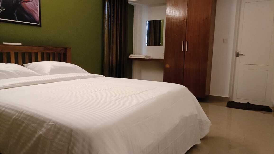 Quarto de hotel com cama grande, cabeceira de madeira, mesa de cabeceira pequena, espelho e guarda-roupa.