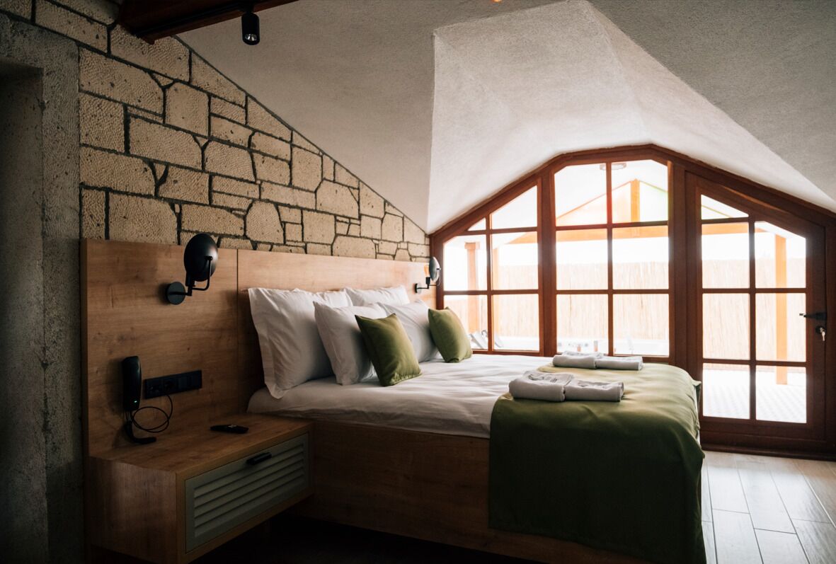 Quarto com parede de pedra, cabeceira de madeira e uma janela grande.