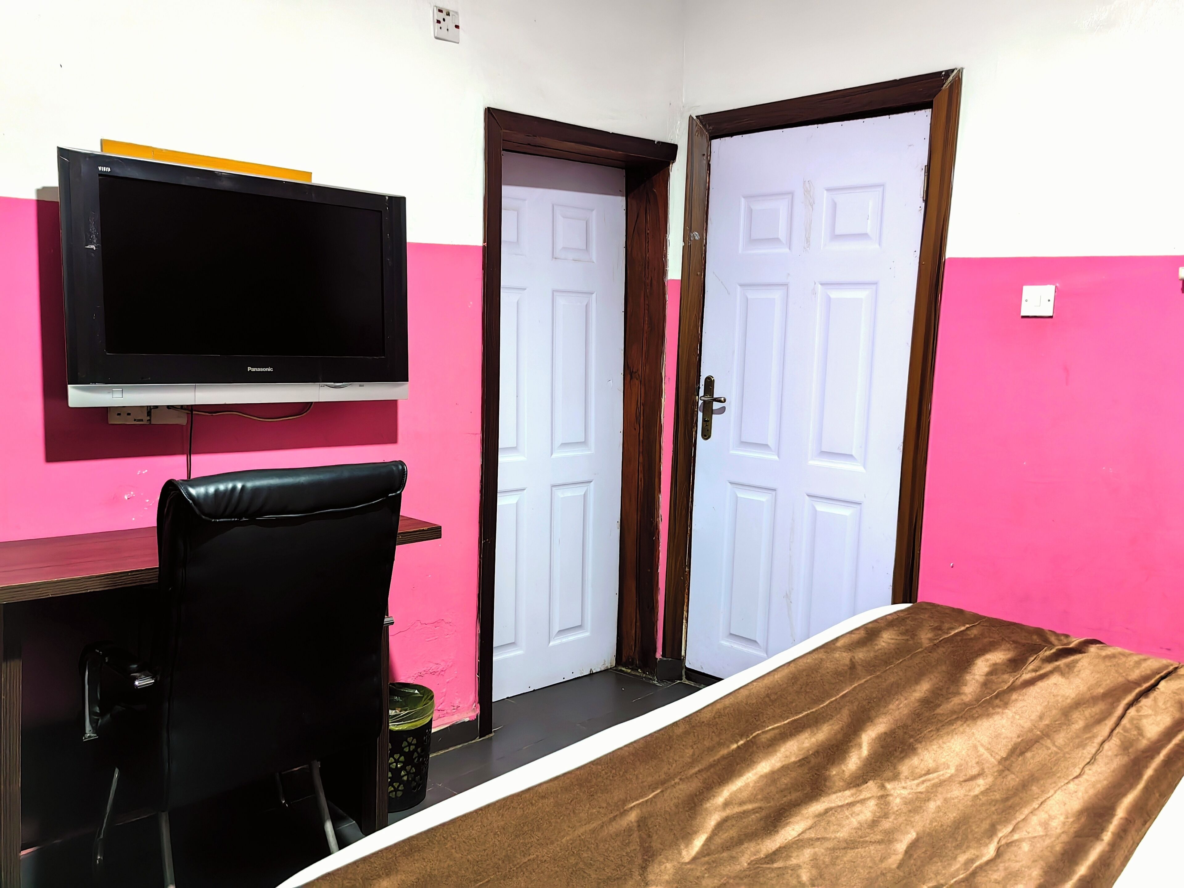 Quarto com cama, escrivaninha, cadeira, televisão e porta.