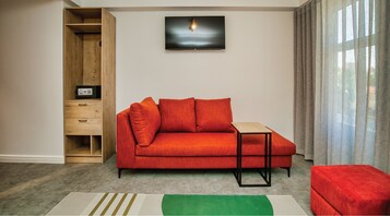 Uma sala de estar moderna com um sofá vermelho, uma mesa de madeira pequena e uma televisão na parede.