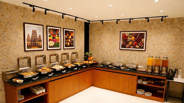 Disposição de buffet com diversos alimentos e bebidas, obras de arte nas paredes e um balcão de madeira.